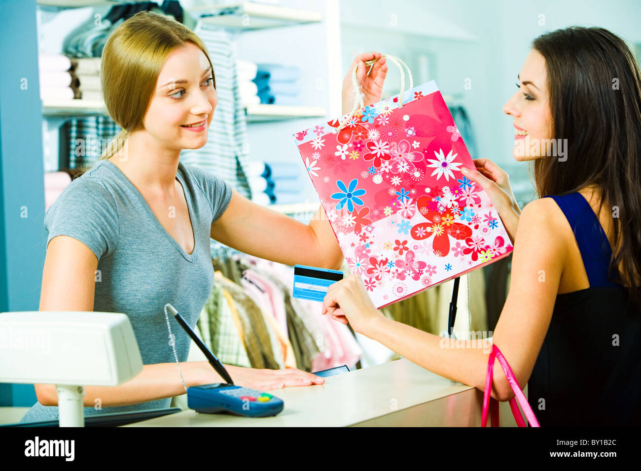 Photo of a friendly salesperson giving shopping bag to pretty customer ...