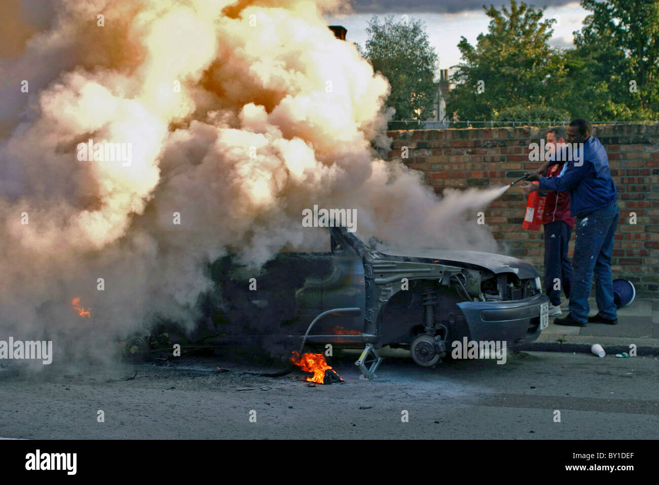 Two people trying to extinguish a car fire Stock Photo - Alamy