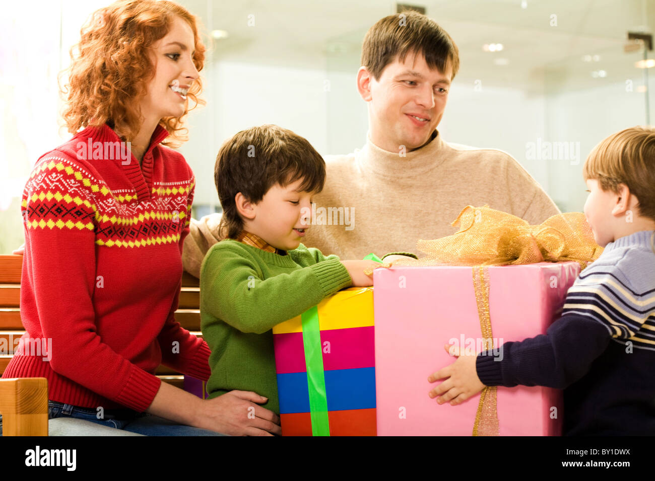 Happy parents looking at their children while they trying to unwrap ...
