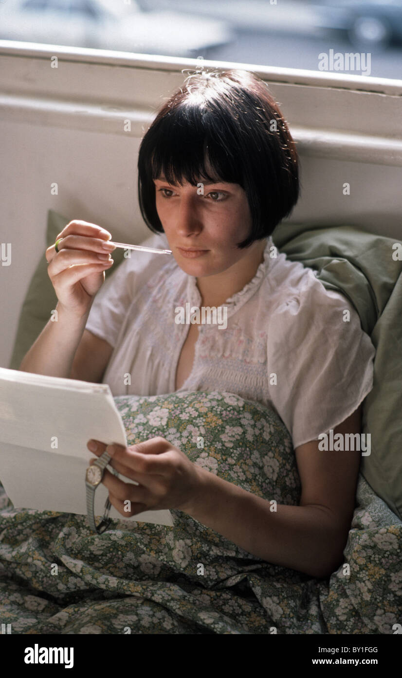young woman taking her temperature in bed as part of her birth control ...