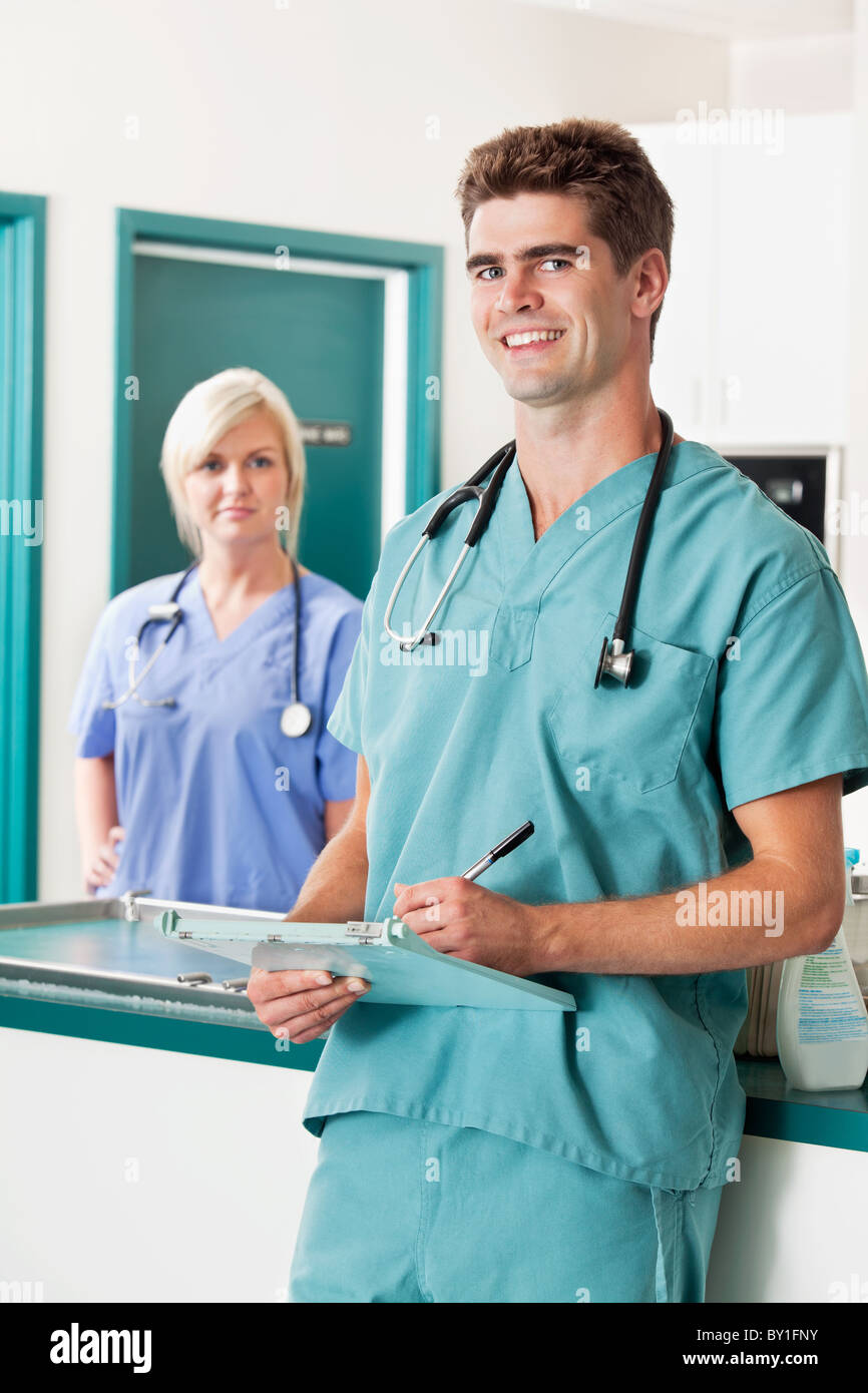 Portrait of smiling male veterinarian with clipboard while assistant in ...
