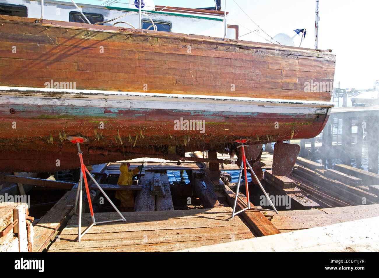 Boat yard worker power washes hull on wooden fishing boat on Rocky Neck ...