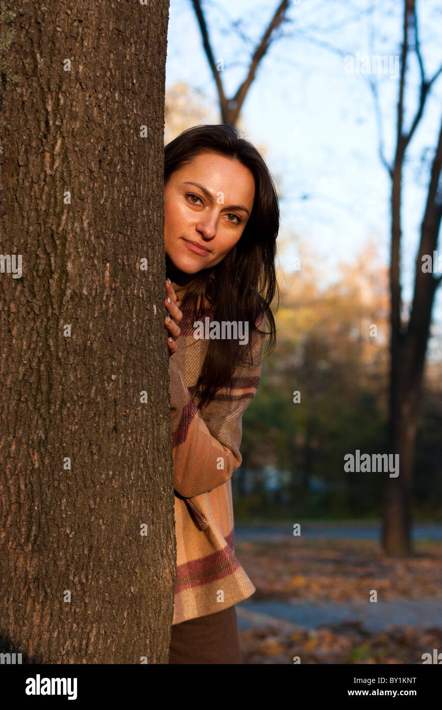 Beautiful young woman looking out behind the tree in autumn Stock Photo ...