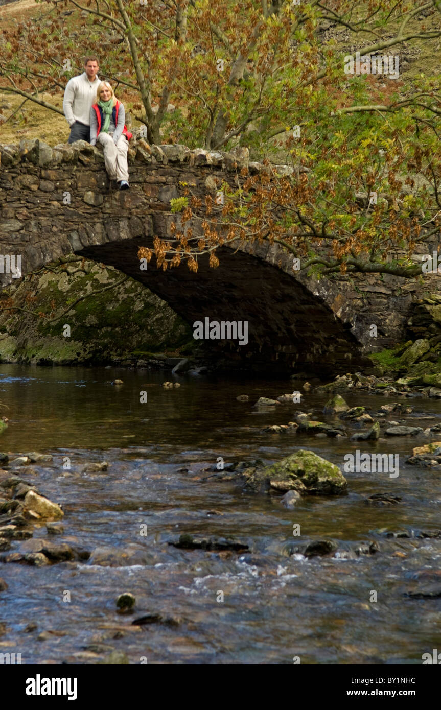UK, North Wales, Snowdonia. A couple relax on an old stone bridge in ...