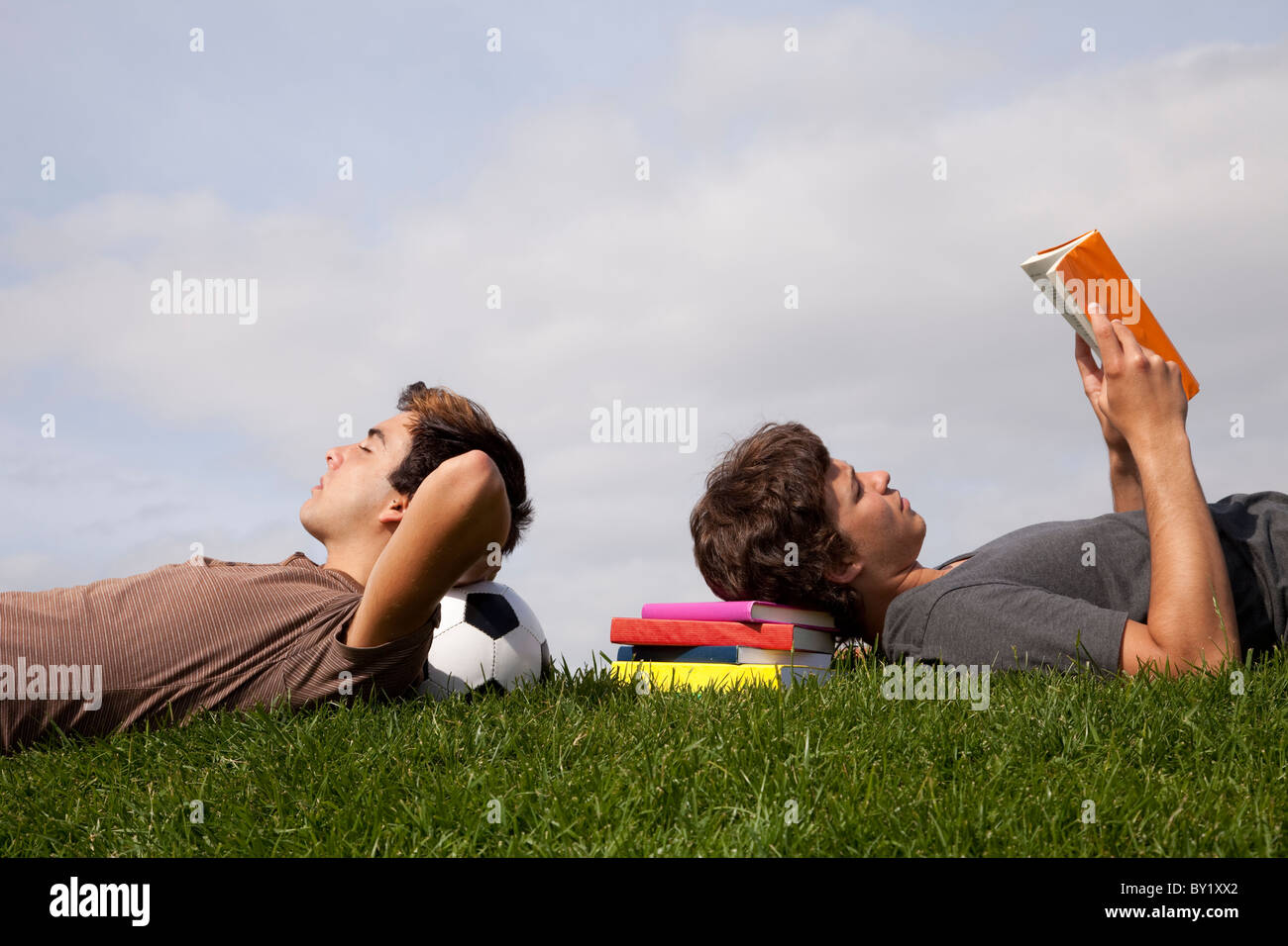 two young students sleeping at the grass over books and a soccer ball ...
