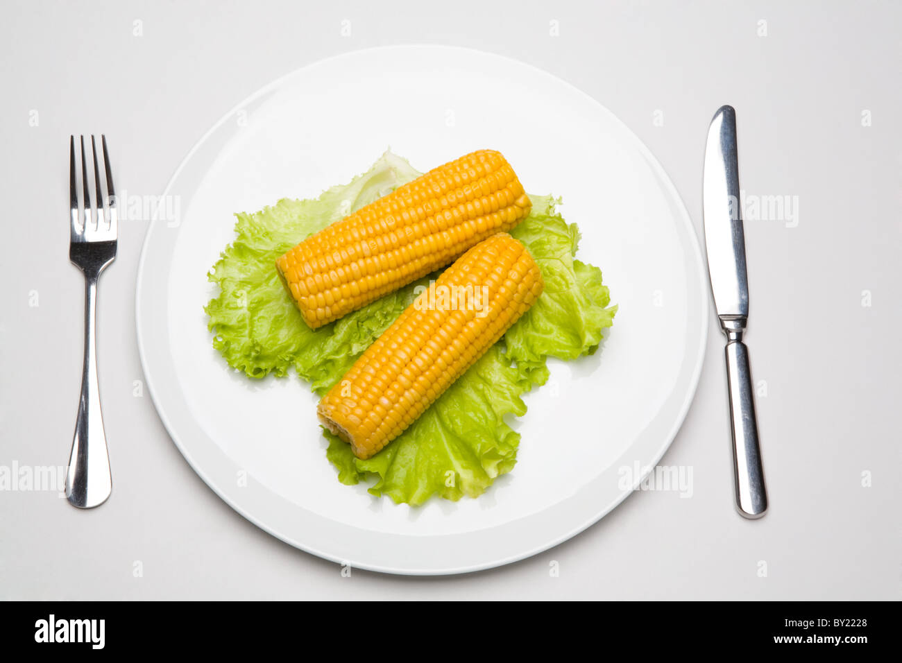 Two ears of corn placed on the plate with fork and knife near by Stock ...