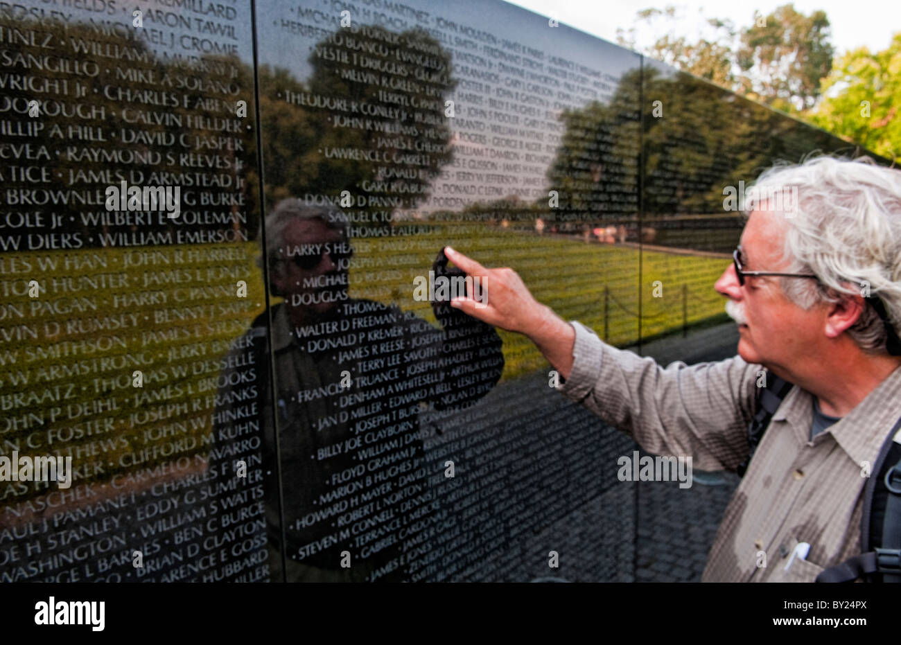 Old soldier looking at friends name at reflections of hero names of war ...