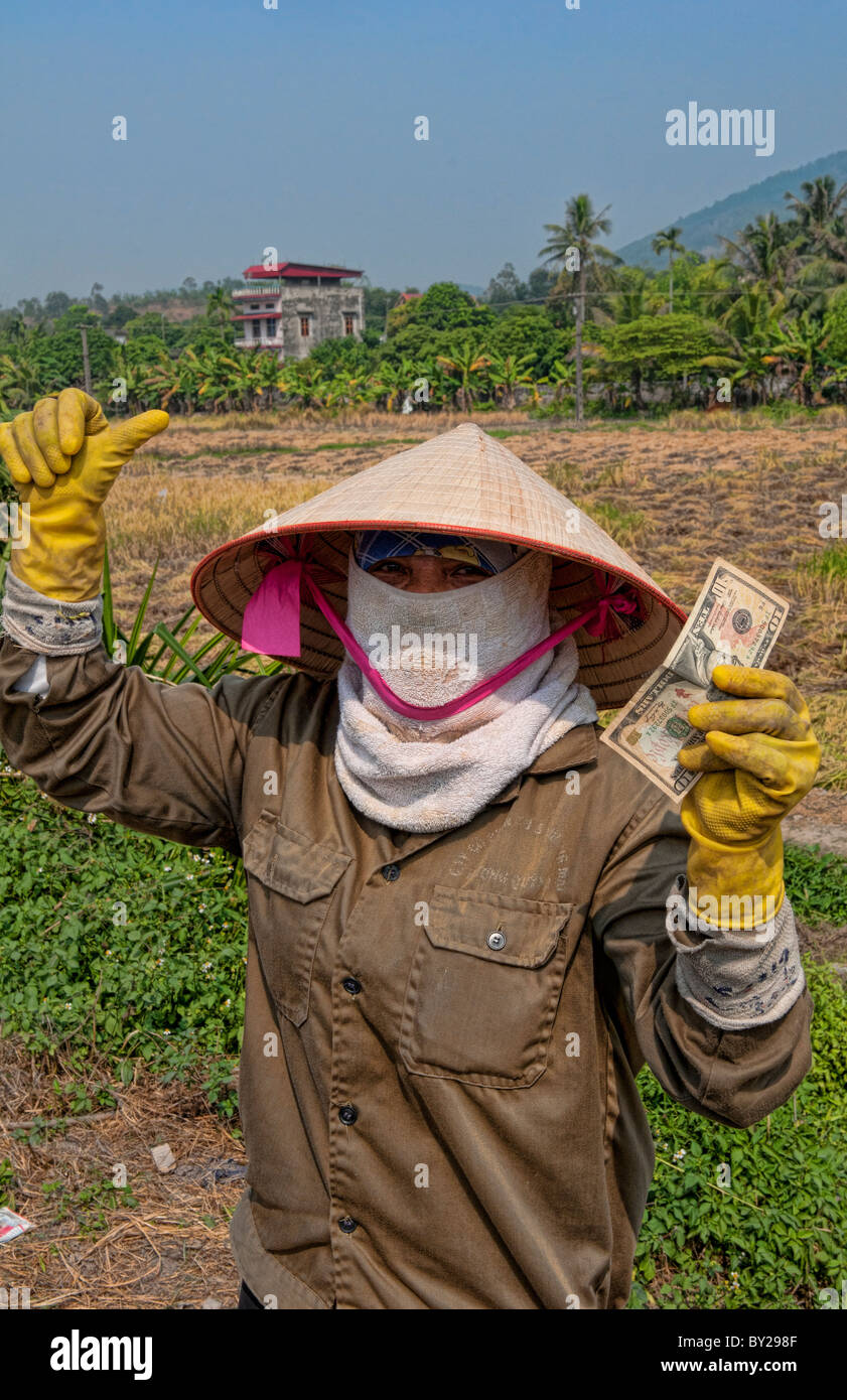 Rice worker with straw hat holding up US $10 bill on farm collecting ...