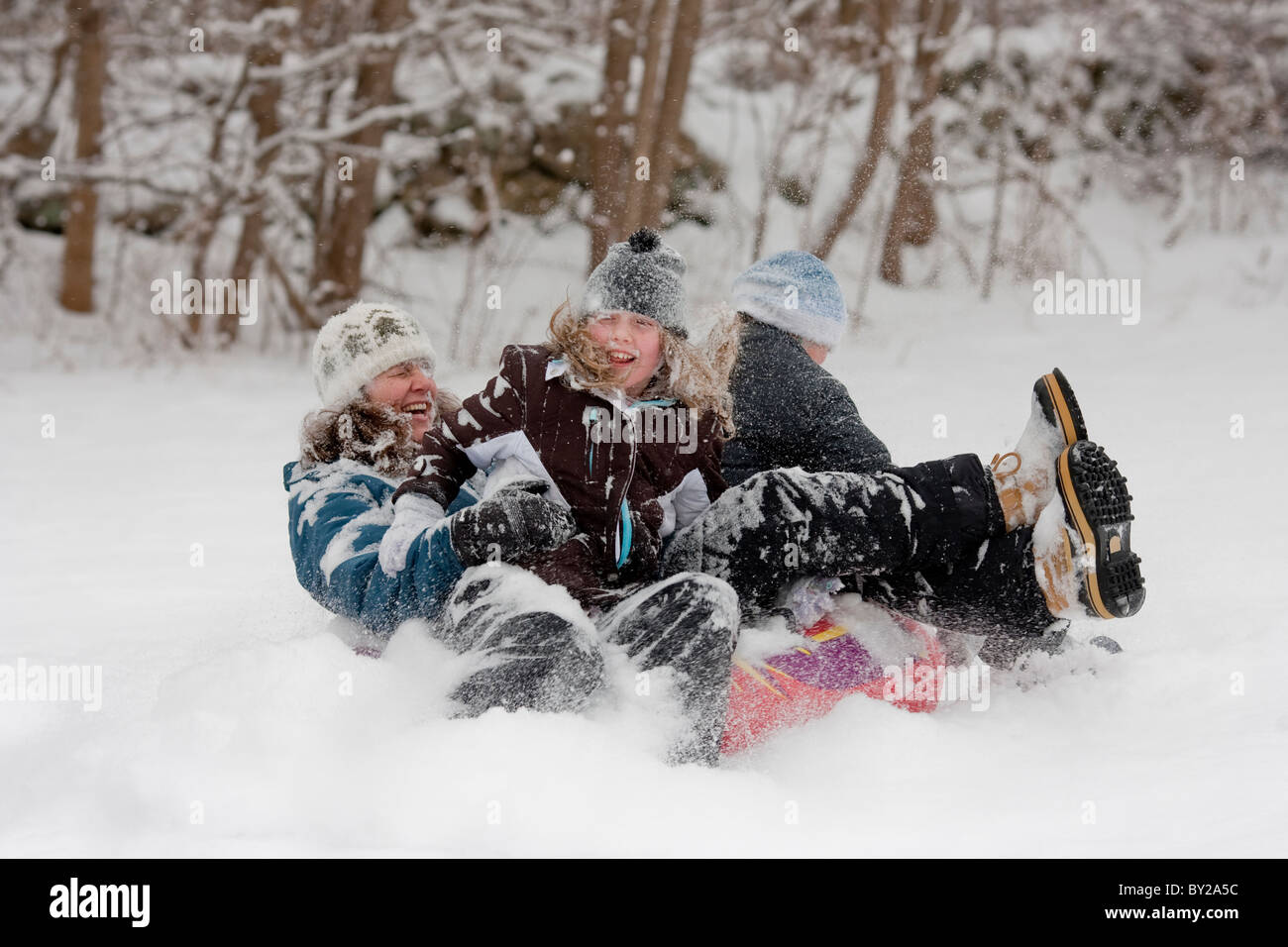 A woman and two children laugh while sledding in deep, powdery snow ...