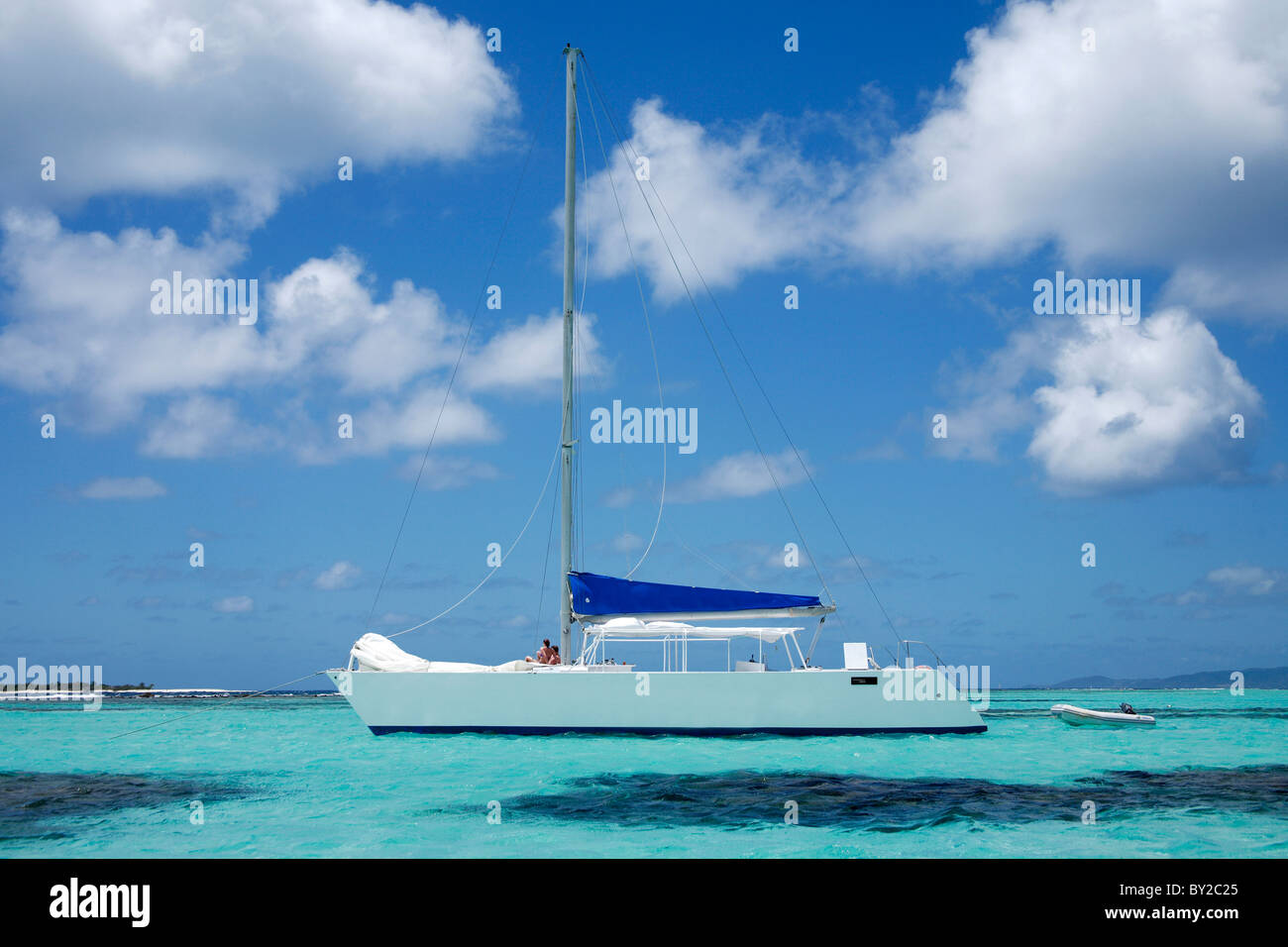 Sailing boat at anchor in the Caribbean with a couple sun bathing on ...