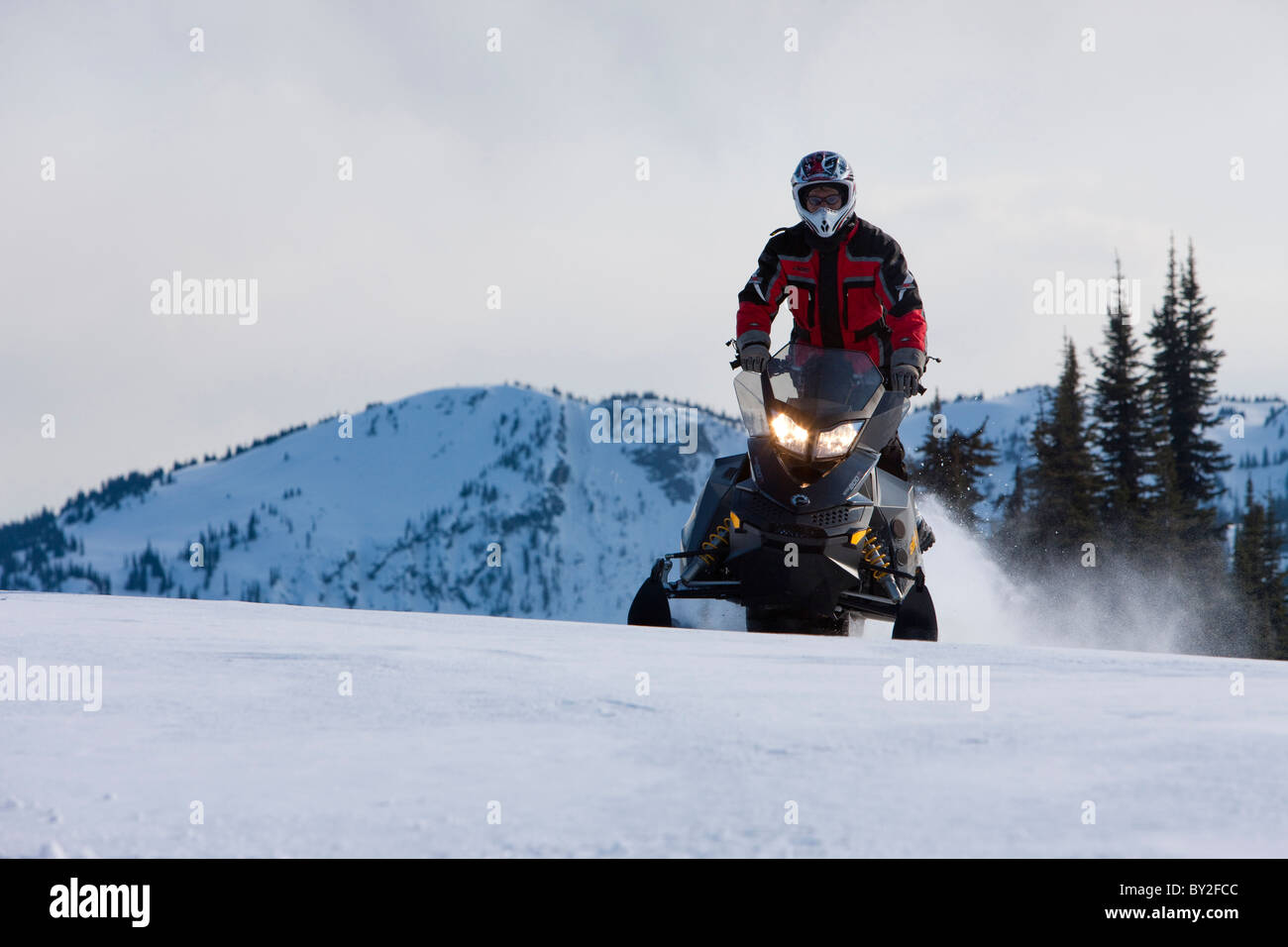 A man rides a snowmobile in a standing position through the snow on ...