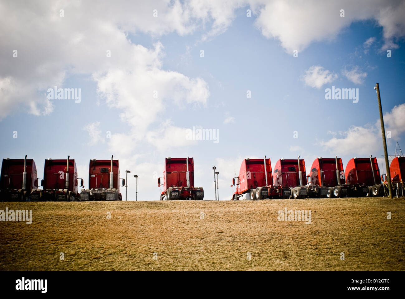 Red tractor trailer trucks aligned and parked on top of a hill in ...