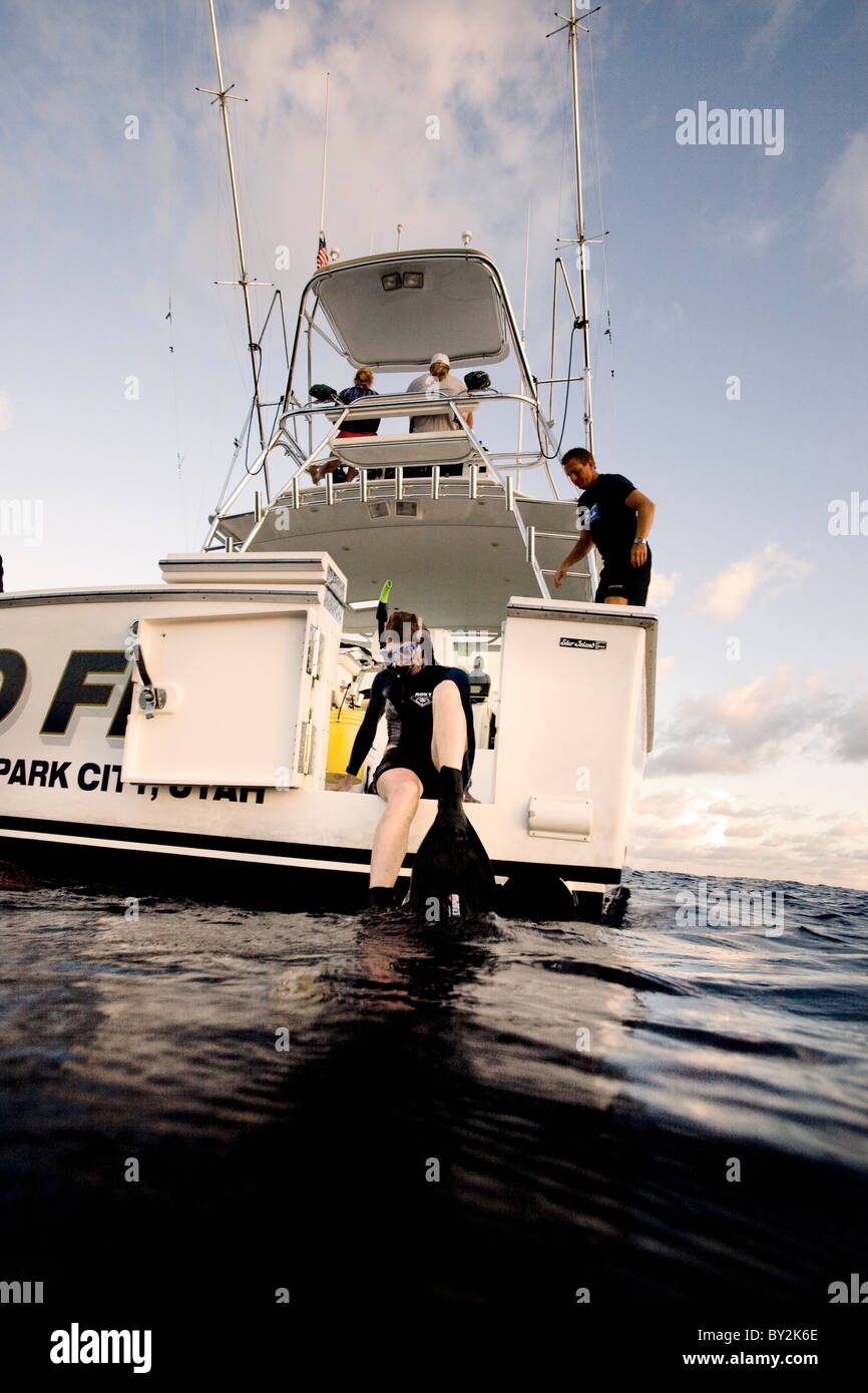 A woman sits on the edge of a boat's dive door, preparing for a dive in ...