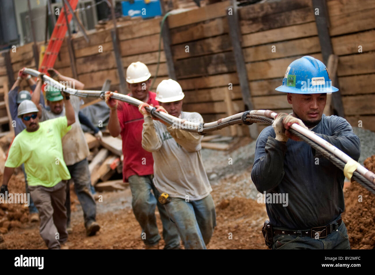 Construction workers carry a long piece of cable on a job site in ...