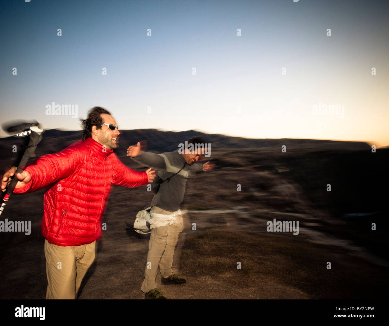 Two men stretch out their arms and lean into a strong wind above a ...