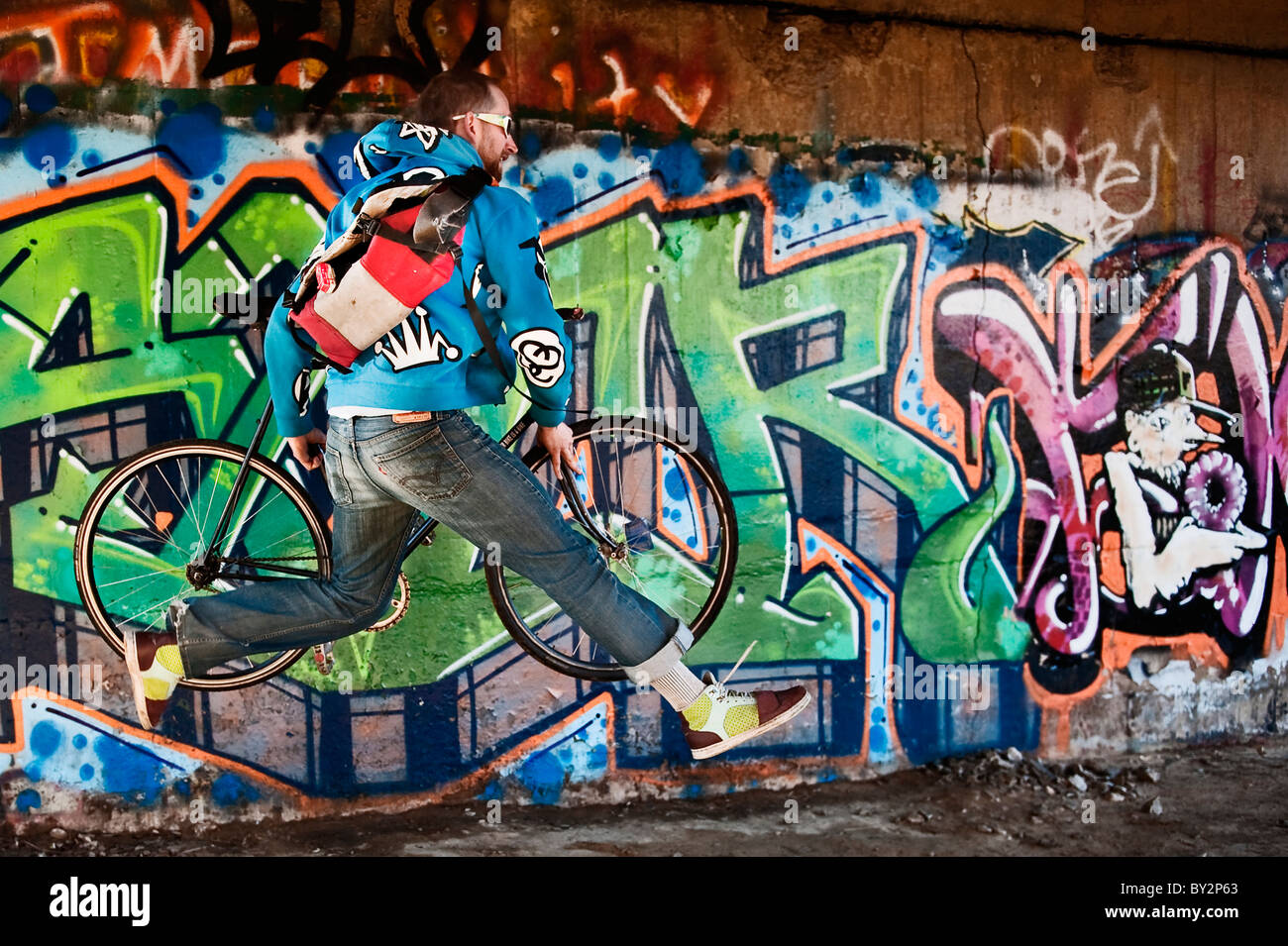 A man jumping with his bicycle in front of a graffiti painted wall ...
