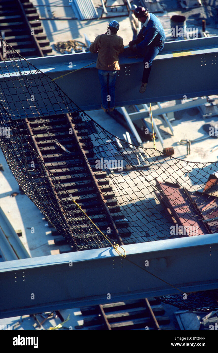 Two workers on beam at commercial construction site with safety nets ...