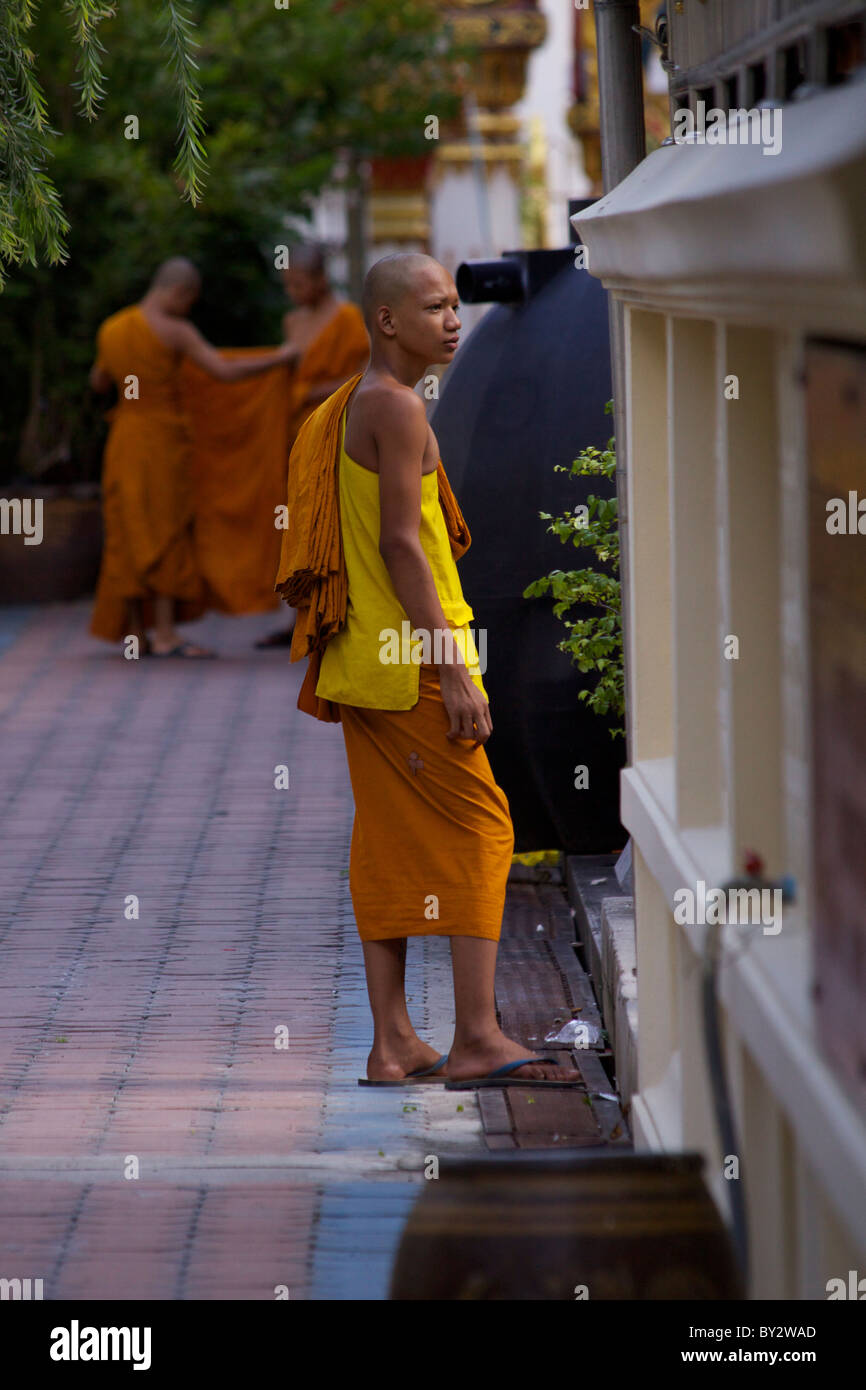 A novice monk in saffron robes waits to enter the building at the Wat ...