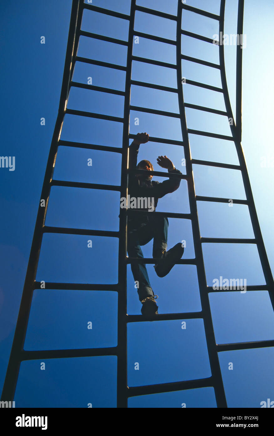 View from below looking up at silhouette of young boy clambering up ...