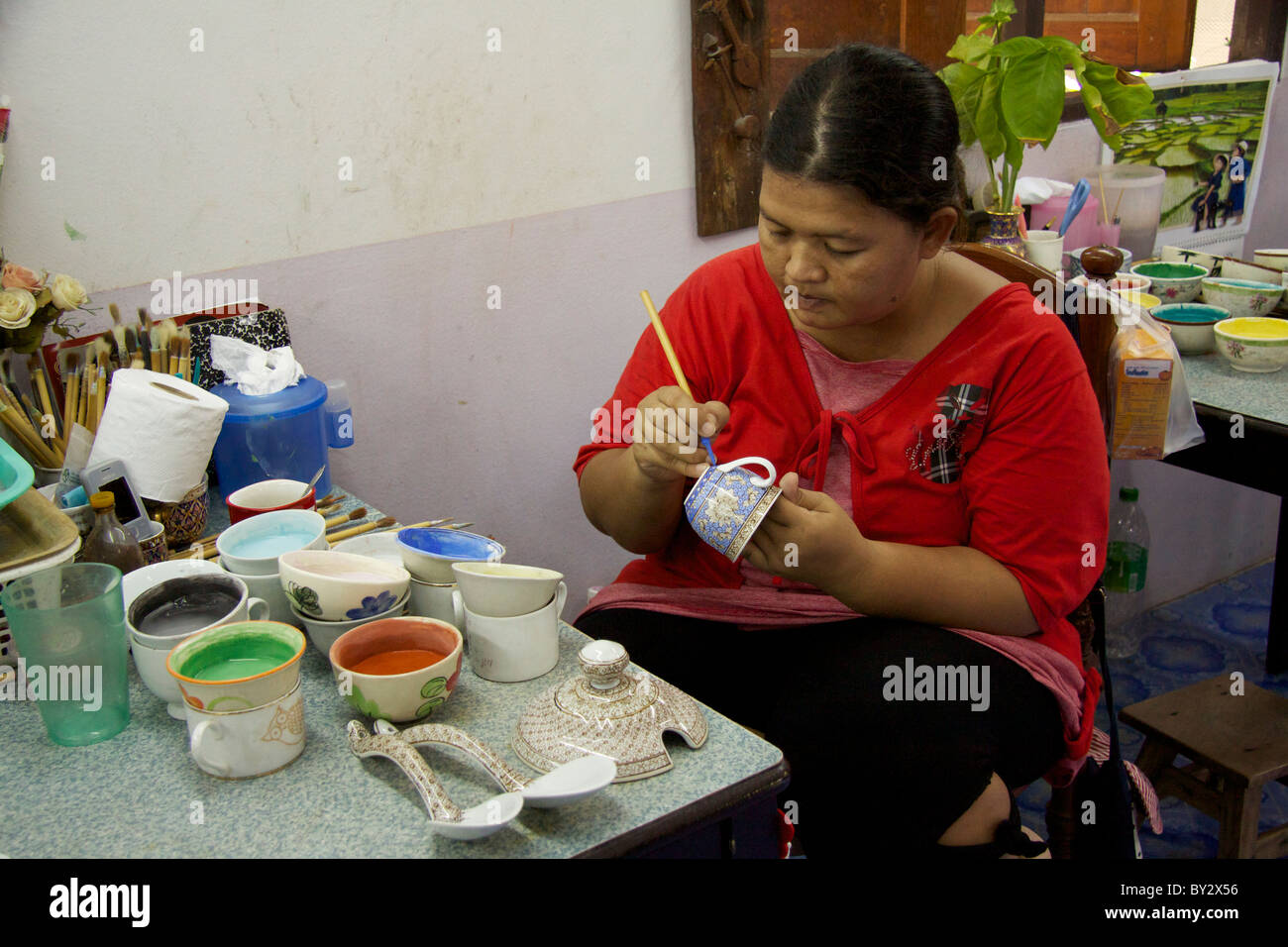 A woman paints Benjarong porcelain cups with glazes in the Don Kai Dee ...