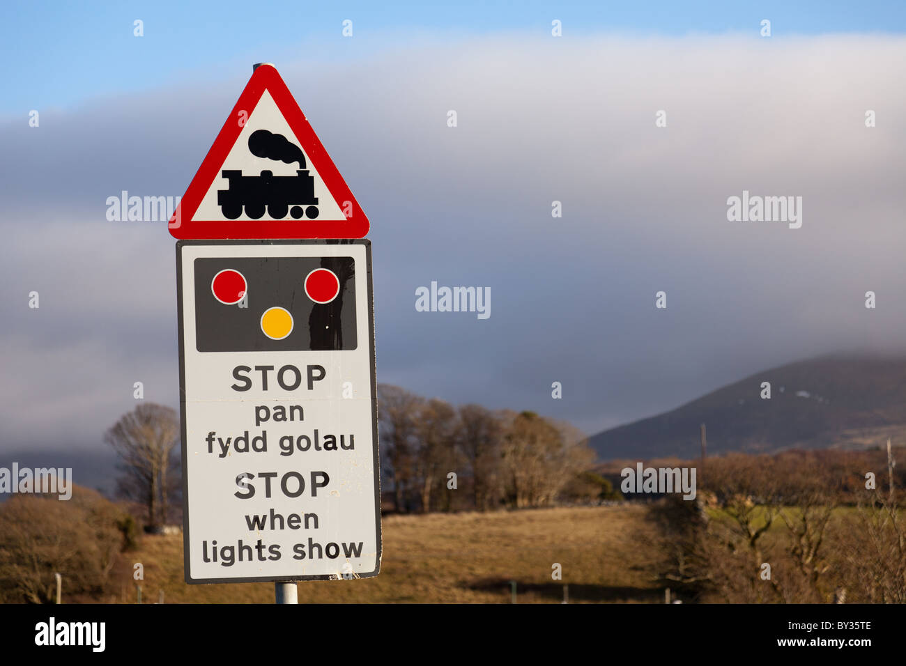 A bilingual Welsh/English road sign showing a level crossing ahead ...