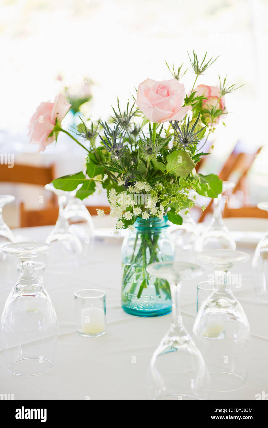 Vase of roses on set dinner table with glasses Stock Photo - Alamy