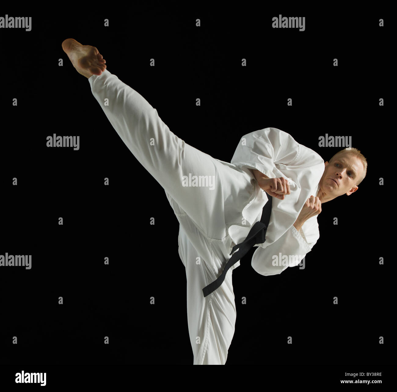 Young man performing karate kick on black background Stock Photo - Alamy