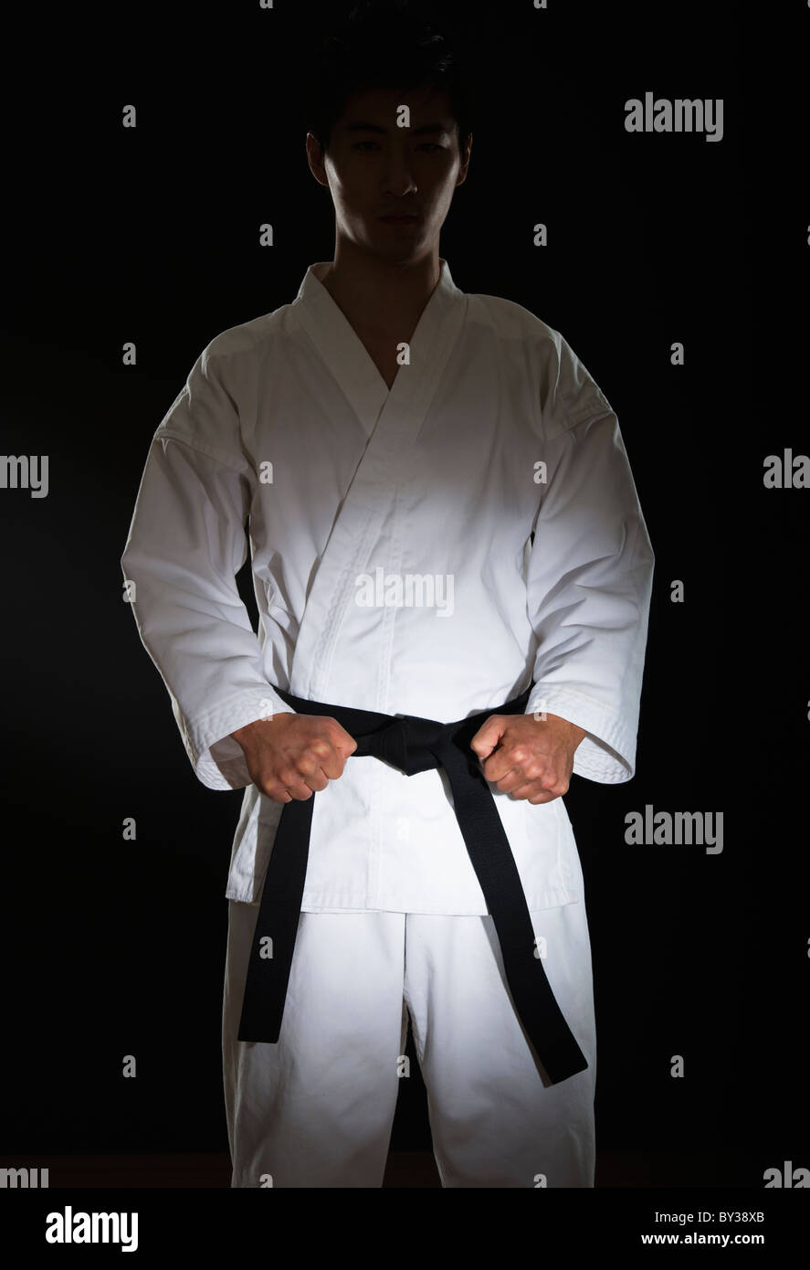 Portrait of young man performing karate stance on black background ...