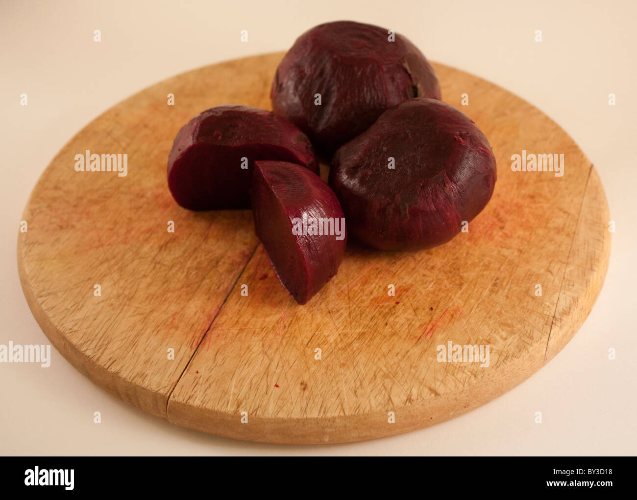 two whole and one halved cooked and peeled beetroot on a round wooden ...