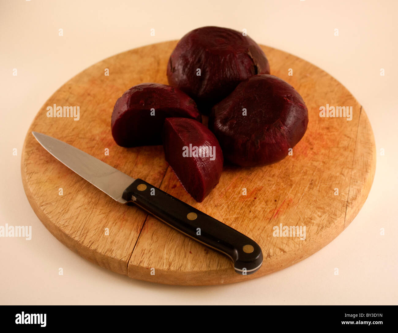 two whole and one halved cooked and peeled beetroot on a round wooden ...
