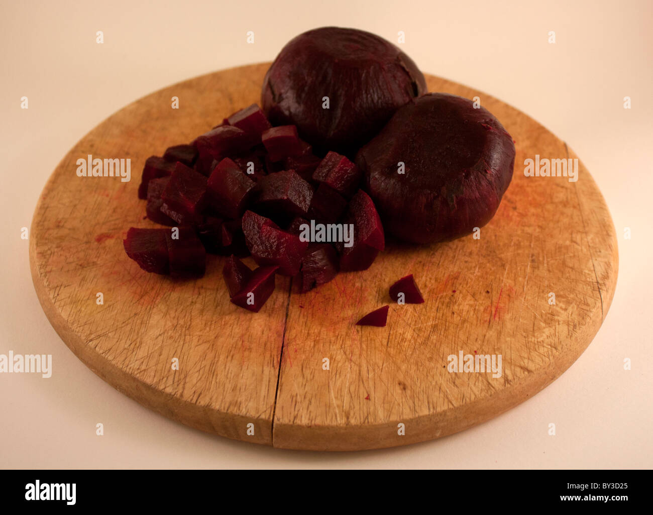 two whole one cooked and peeled chopped beetroot on a round wooden ...