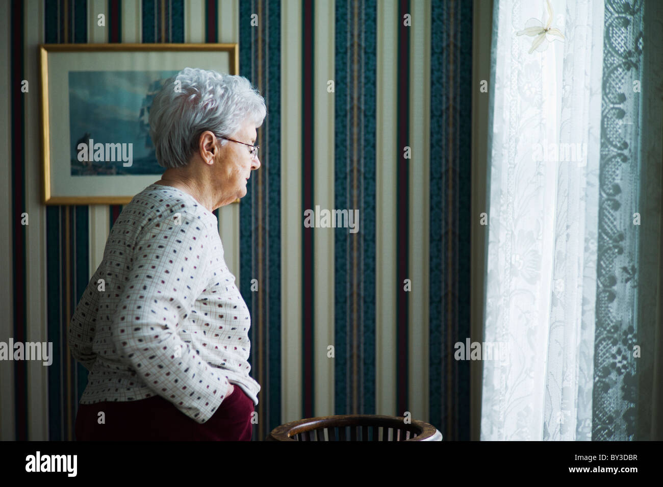 Old woman stands looking out window Stock Photo - Alamy