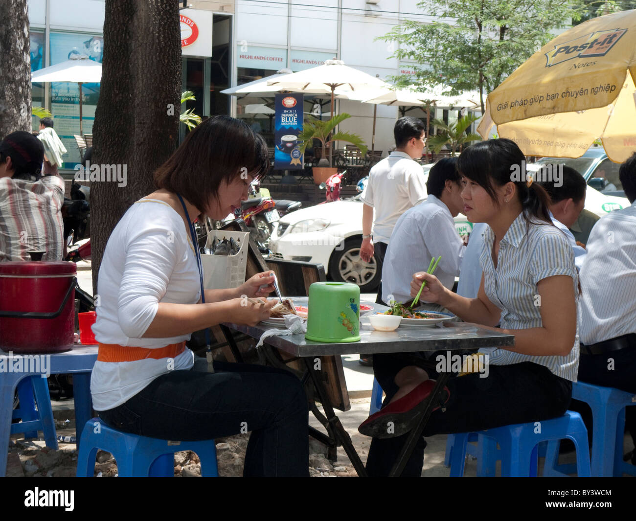 Vietnamese people and tourists sit at tables and eat at outdoor street ...