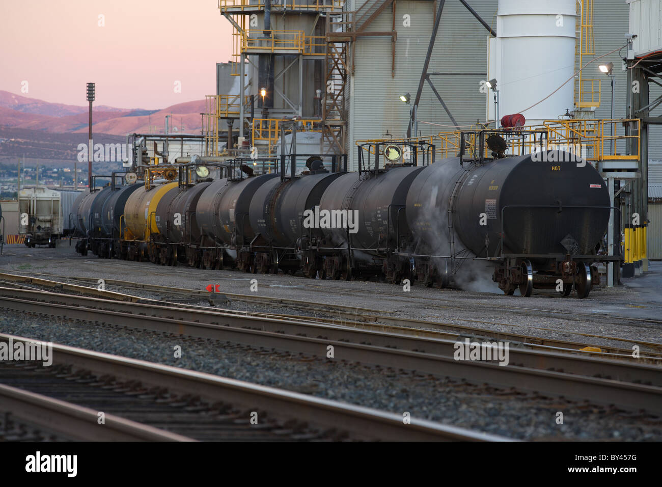 A row of railroad tanker cars being unloaded at an industrial facility ...