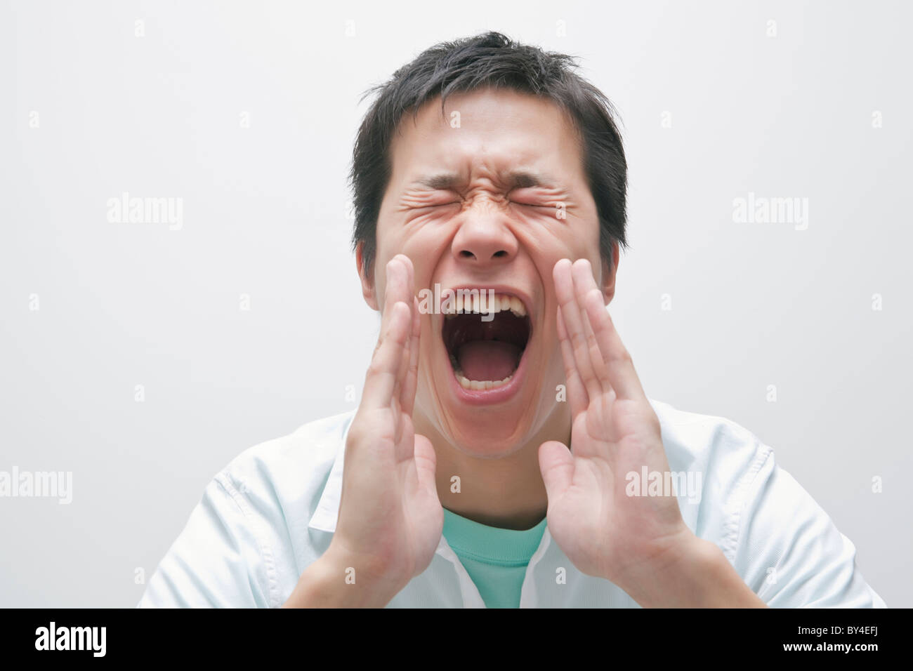 Young man shouting with hands covering mouth Stock Photo - Alamy