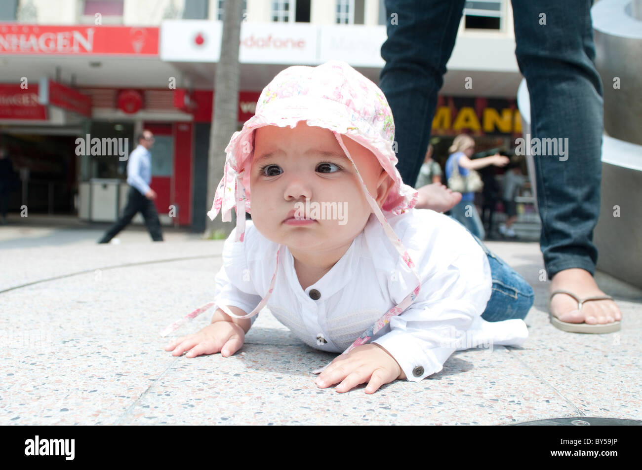 Ten month old baby girl crawling with her mother behind watching over ...