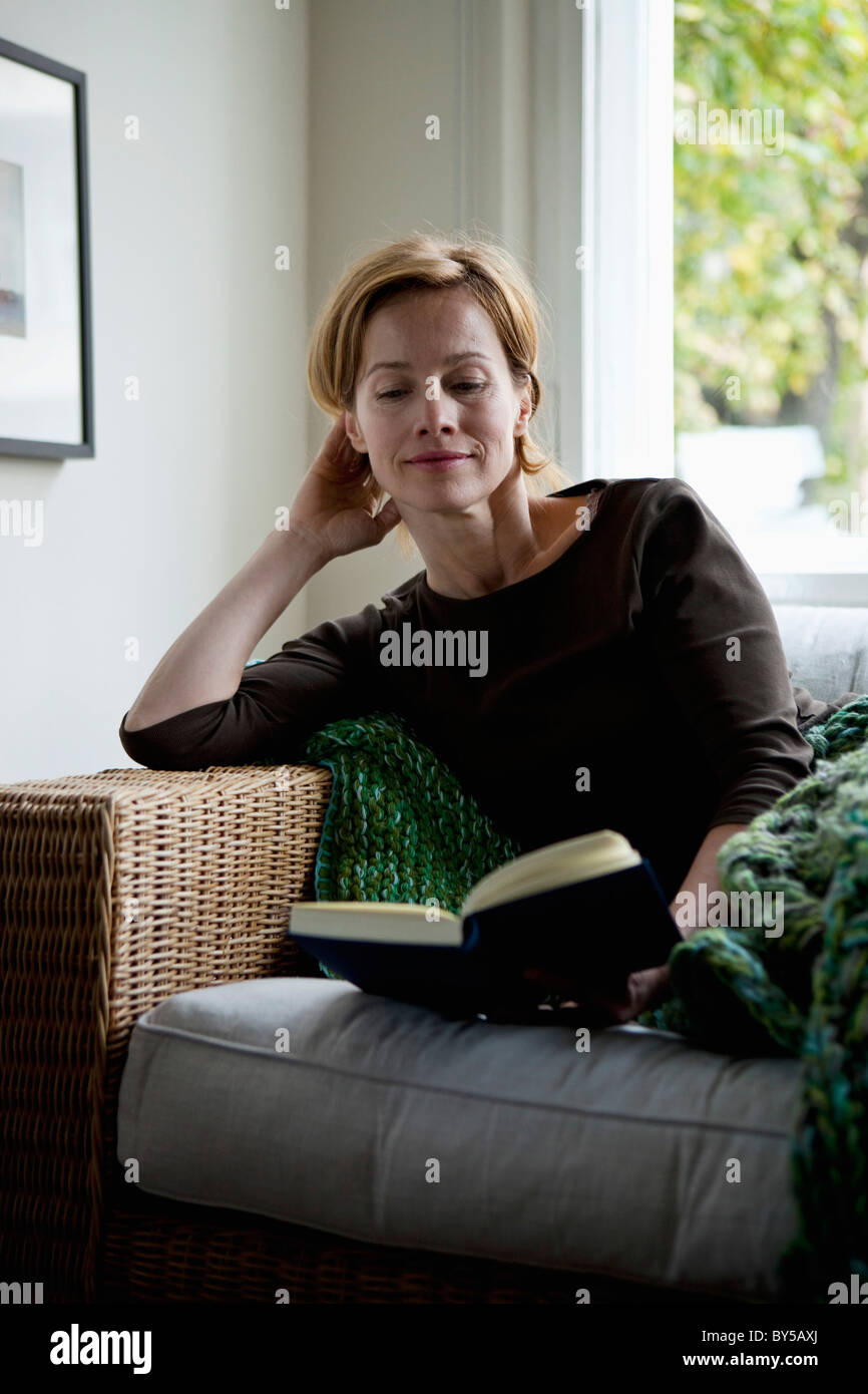 A woman reading a book while reclining on a sofa Stock Photo - Alamy