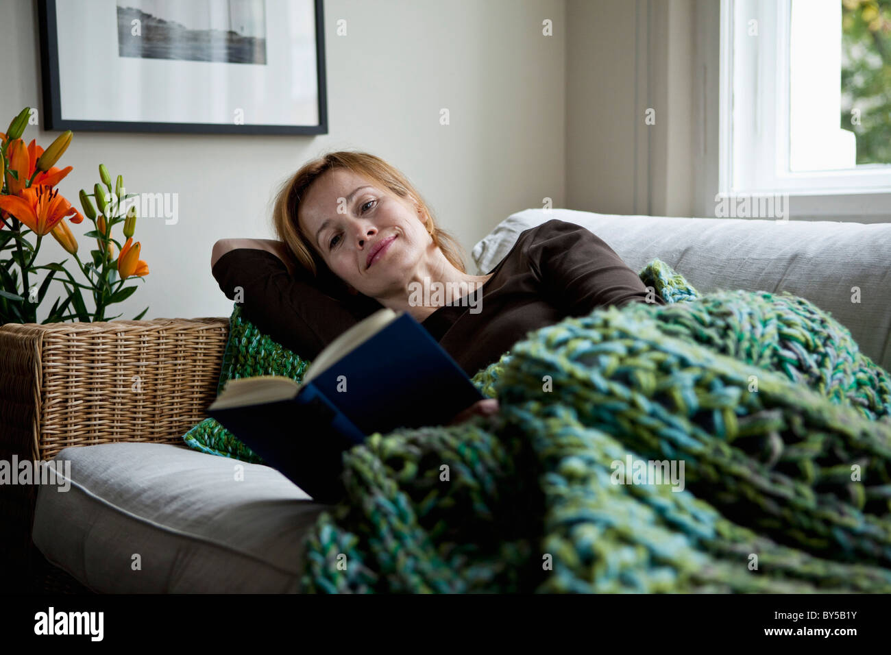 A woman reading a book while reclining on a sofa Stock Photo - Alamy