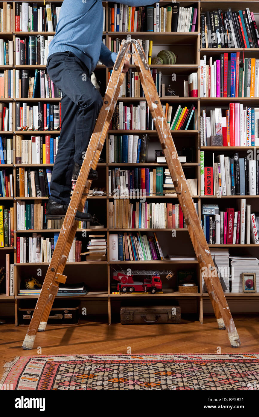 A man climbing up a ladder in a home library Stock Photo - Alamy