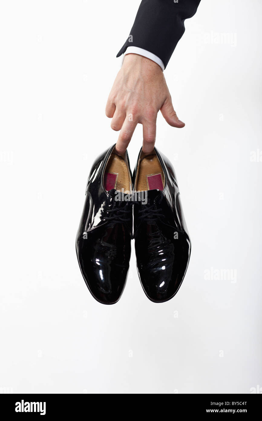 A man holding a pair of patent leather dress shoes, focus on hand Stock ...