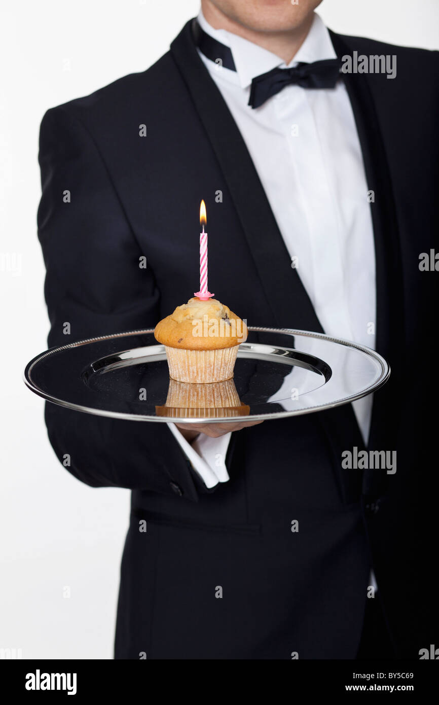 A butler presenting a muffin with a lit birthday candle on a silver ...