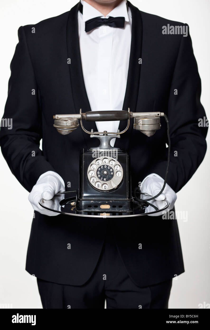A butler holding an antique rotary phone on a silver tray, midsection ...