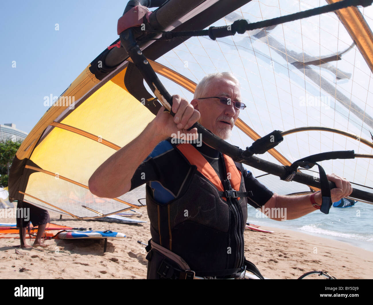 A senior windsurfer carrying his sail down to the beach Stock Photo - Alamy