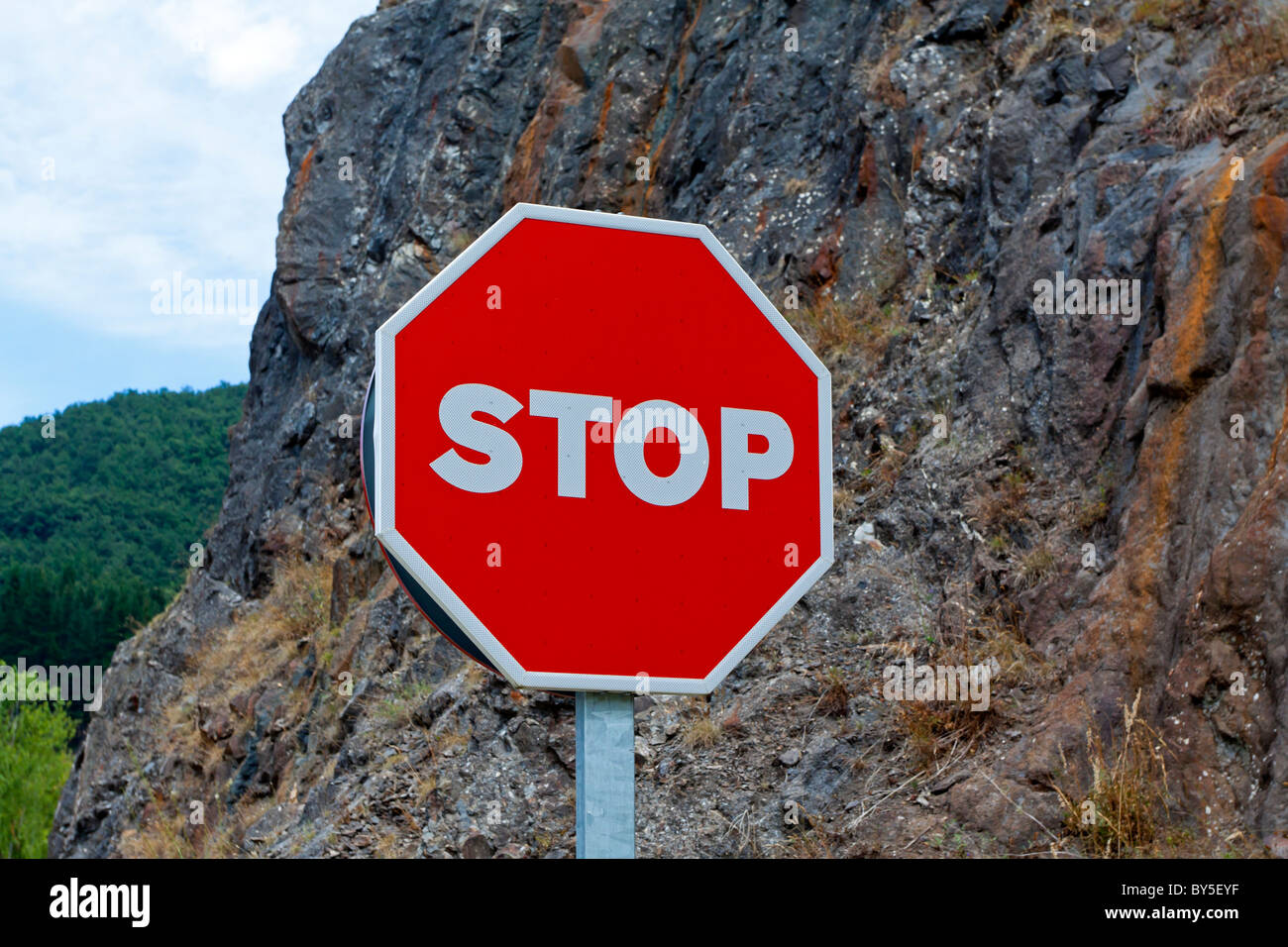 Octagonal red stop sign on a road with rocky cliff behind Stock Photo ...