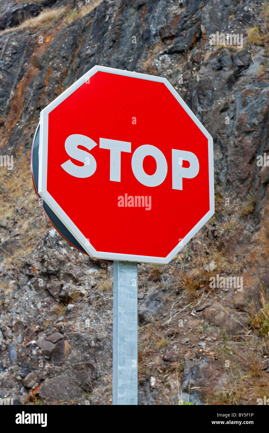 Octagonal red stop sign on a road with rocky cliff behind Stock Photo ...
