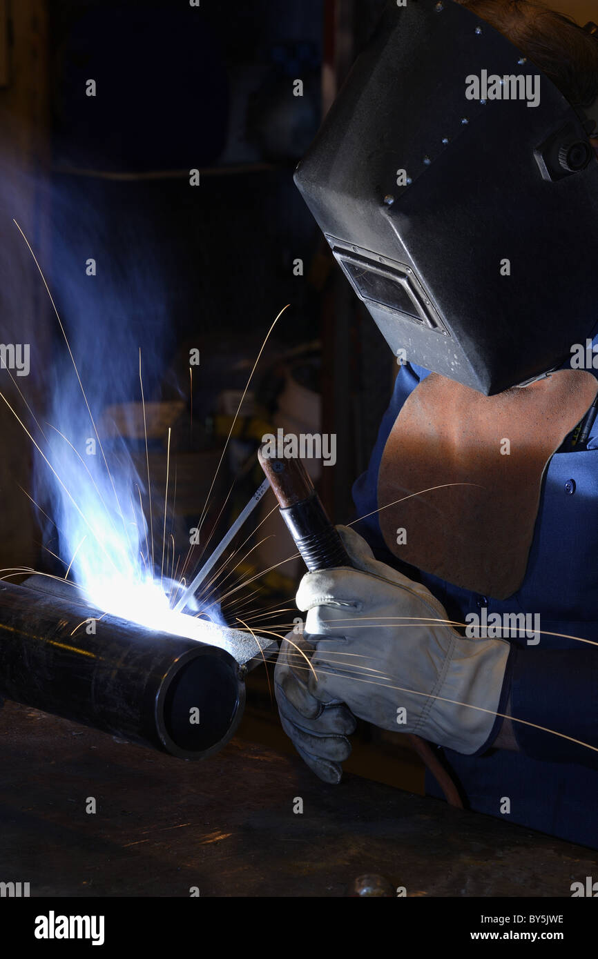 A man arc welding. Sparks are flying through the air, and smoke is ...
