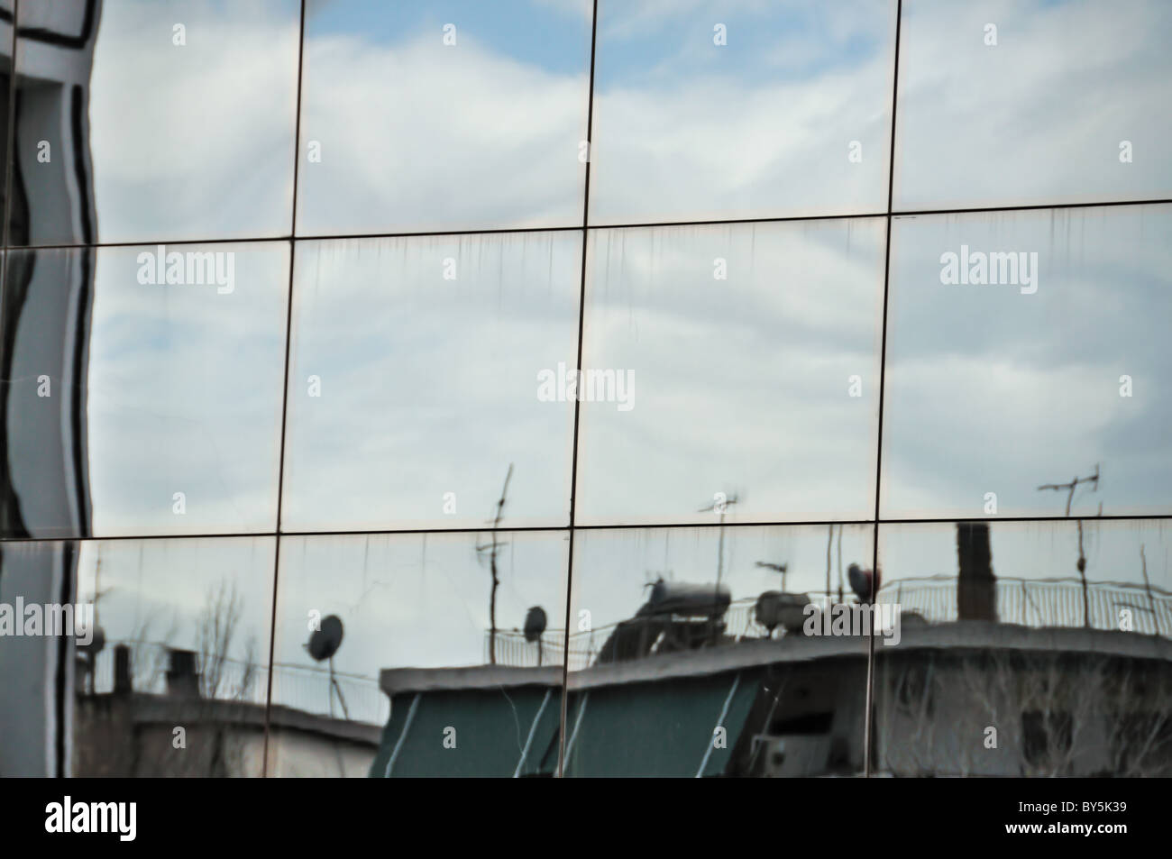 Building rooftops and moody sky mirrored on glass facade Stock Photo ...