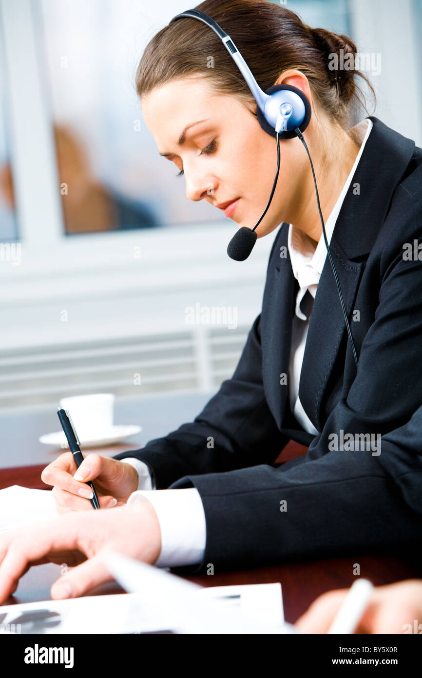 Portrait of telephone operator with headset writing something in the ...