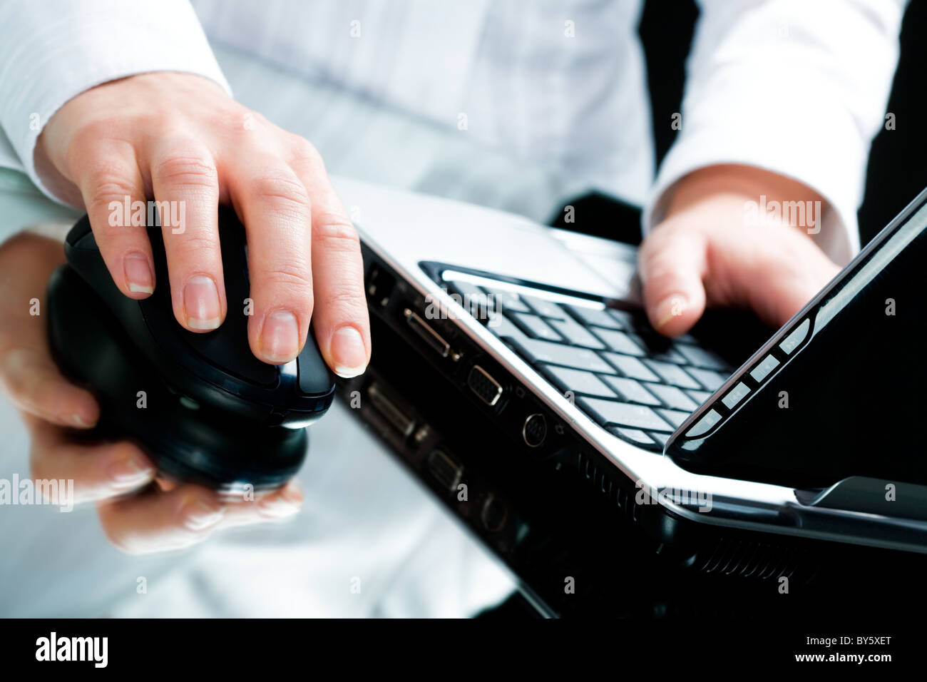 Closeup of woman’s hand on the mouse while her other hand pressing a ...