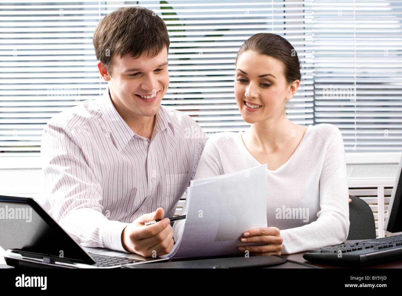 Image of two confident people reading a document together in the office ...